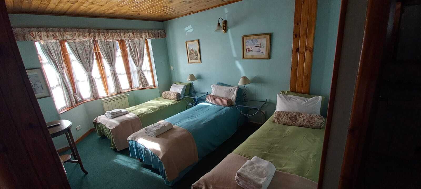 Quarto com duas camas individuais, uma pequena mesa e janela com cortinas.
