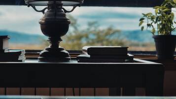 Uma luminária de mesa sobre uma superfície refletora, com o céu ao fundo e uma planta.