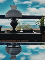 Uma luminária de mesa sobre uma superfície refletora, com o céu ao fundo e uma planta.