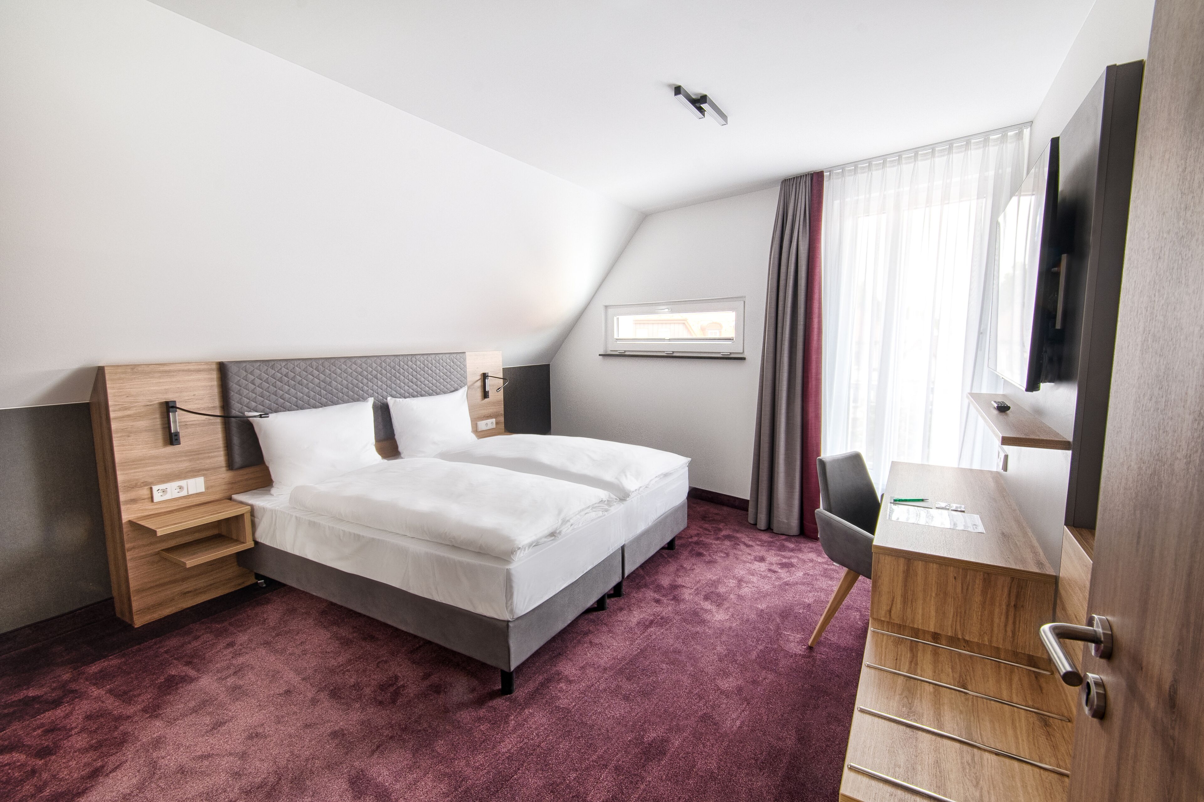 Quarto de hotel moderno com uma cama grande, uma escrivaninha e uma televisão.