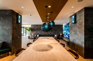 Uma sala de conferências moderna com uma mesa comprida, cadeiras de madeira e uma luminária esférica única.