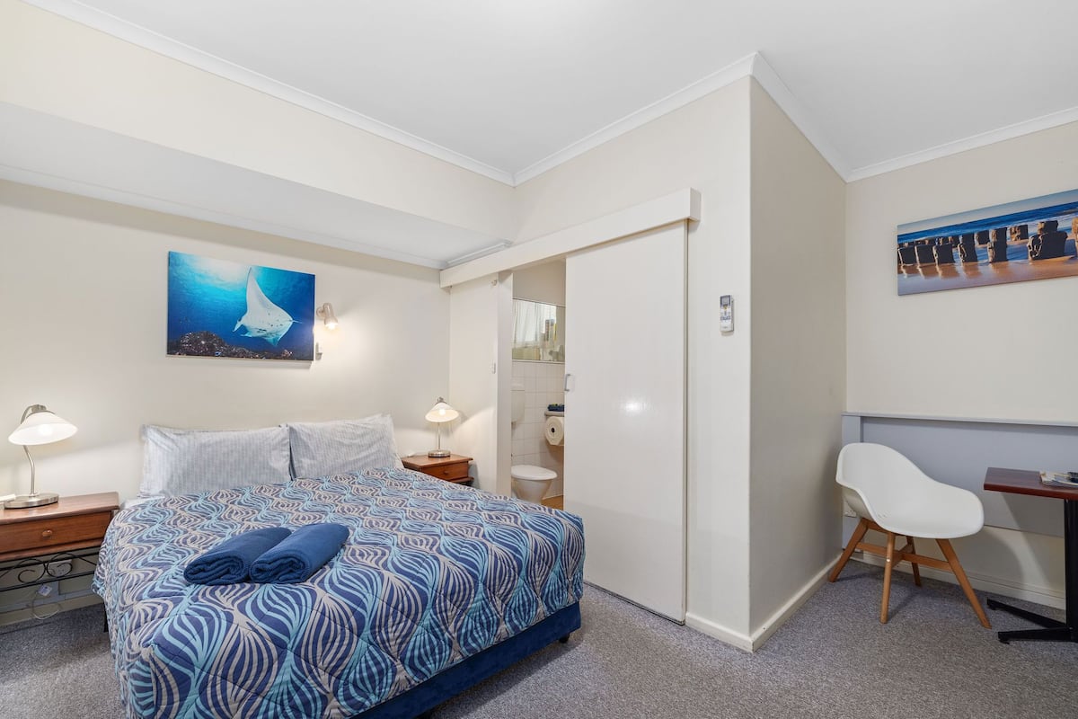 Quarto de hotel com cama, escrivaninha, cadeira e obras de arte nas paredes.