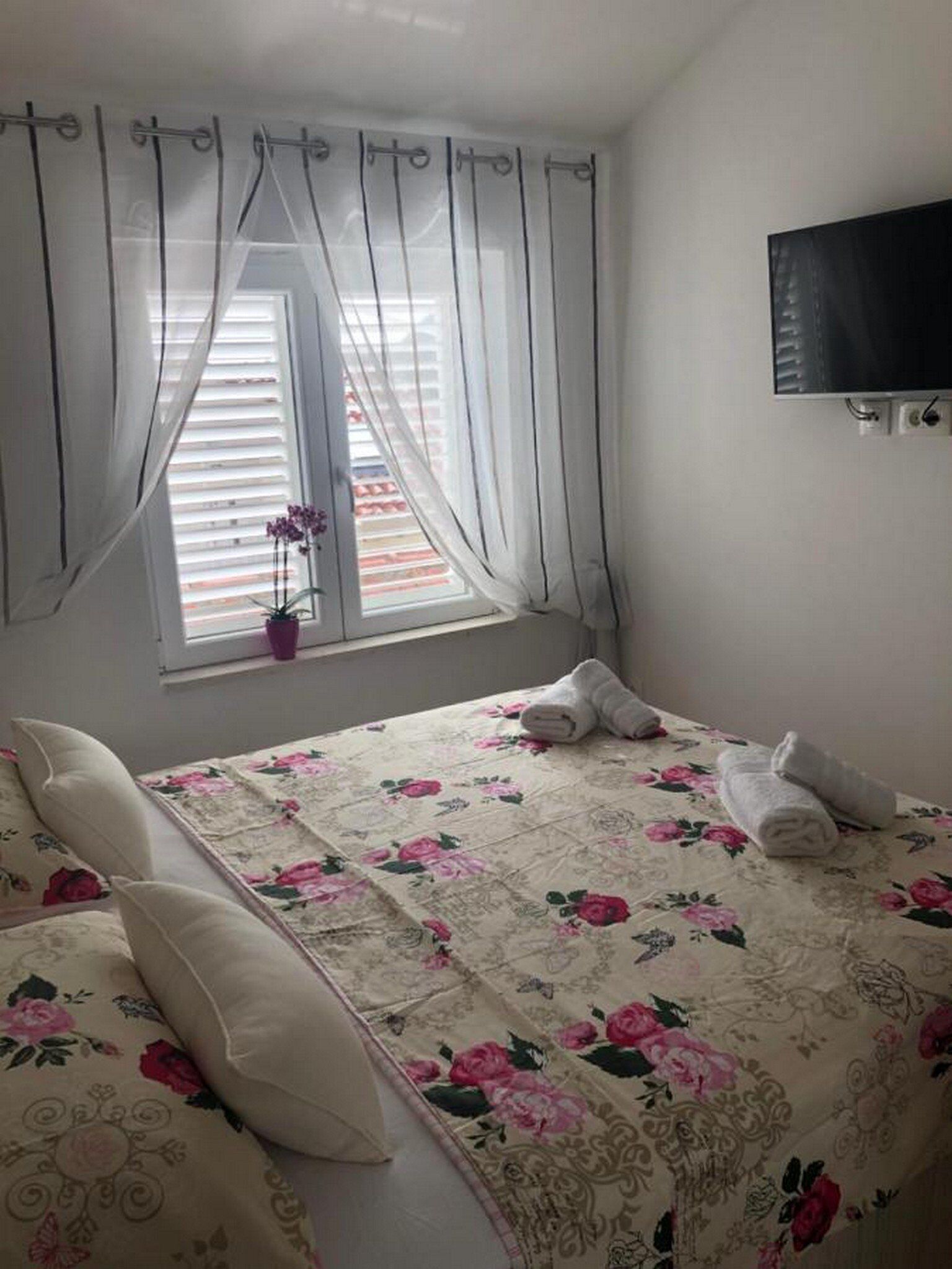 Quarto com cama, almofadas, televisão, janela com cortinas e um vaso de planta.