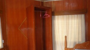 Quarto com guarda-roupa de madeira, cama com cabeceira, mesa com cadeiras e um cabideiro.