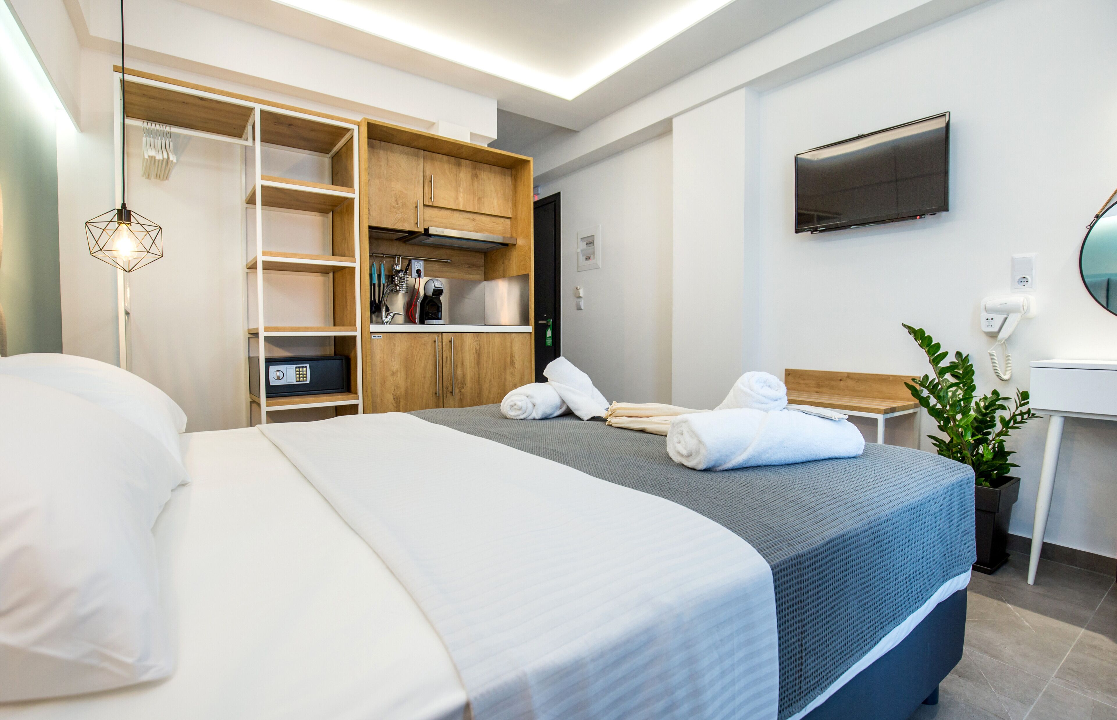 Quarto de hotel moderno com uma cama grande, guarda-roupa embutido, escrivaninha com cadeira, televisão e uma planta em vaso.