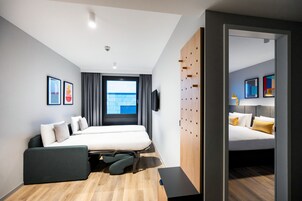 Quarto de hotel moderno com uma cama grande, uma escrivaninha, uma cadeira, uma televisão e uma janela com cortinas.