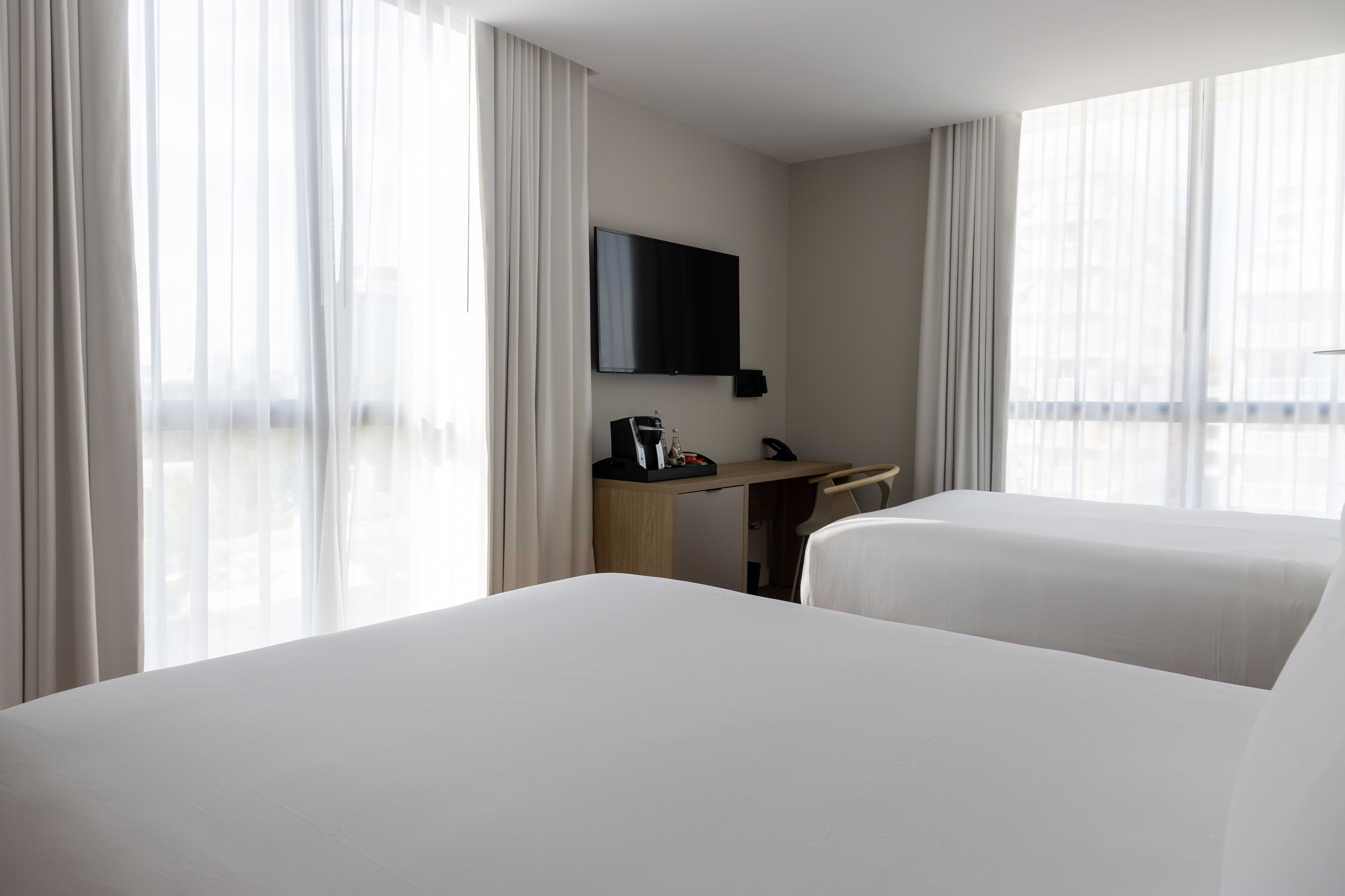 Quarto de hotel com duas camas, uma mesa de trabalho com televisão de tela plana, telefone e máquina de café.