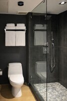 Uma casa de banho moderna com sanita, cabine de duche com vidro e um porta-toalhas com toalhas dobradas.