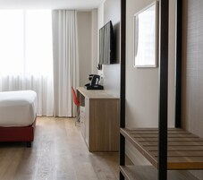 Quarto de hotel com uma cama, secretária, cadeira, televisão e escada.