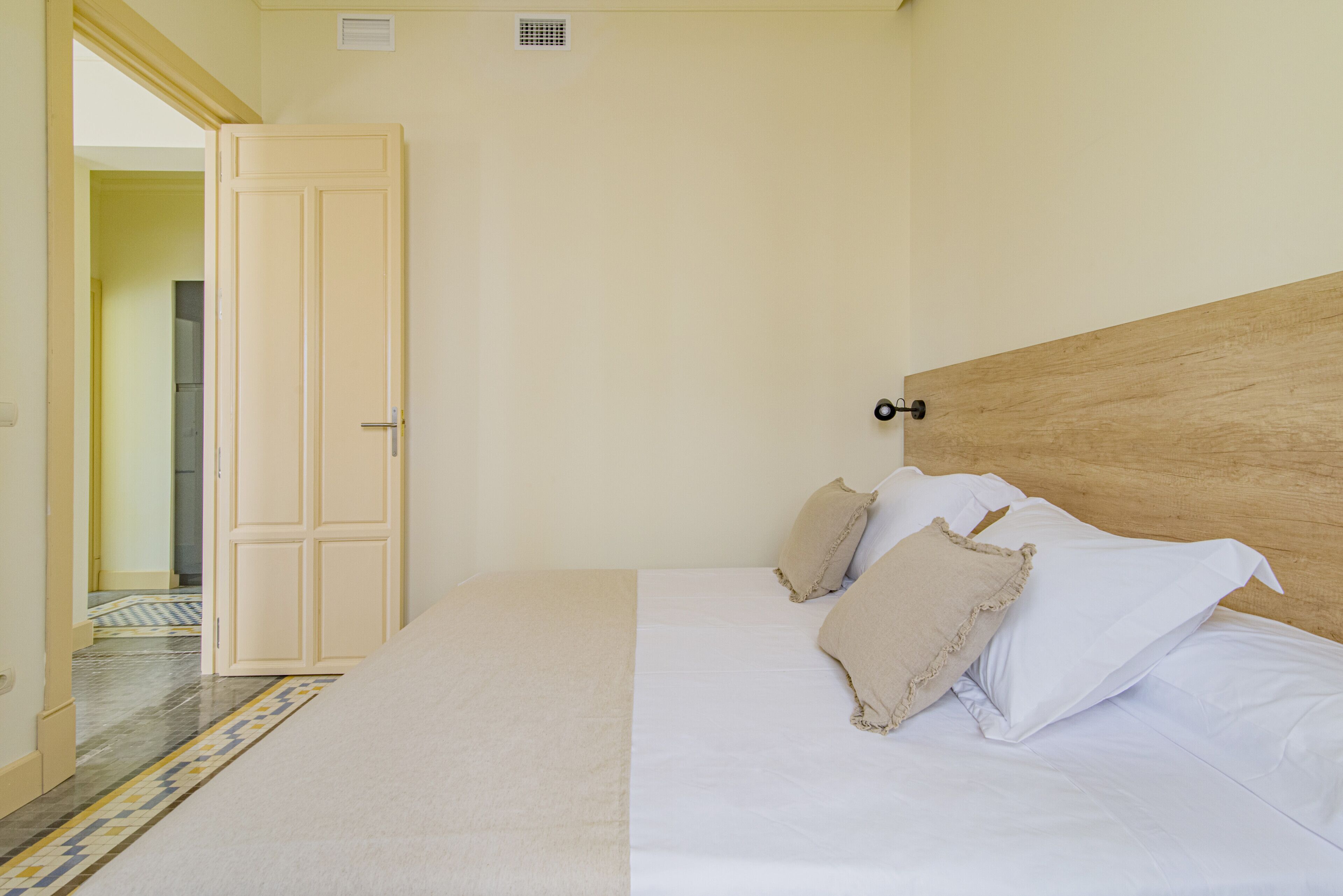 Quarto com cabeceira de madeira, cama com roupa de cama branca e manta bege.