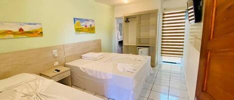 Quarto de hotel com duas camas, uma mesa de cabeceira, um quadro na parede e um banheiro visível através de uma porta de vidro.