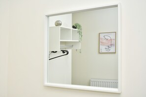 Um quarto com um radiador branco, uma planta pendurada e uma obra de arte emoldurada na parede.