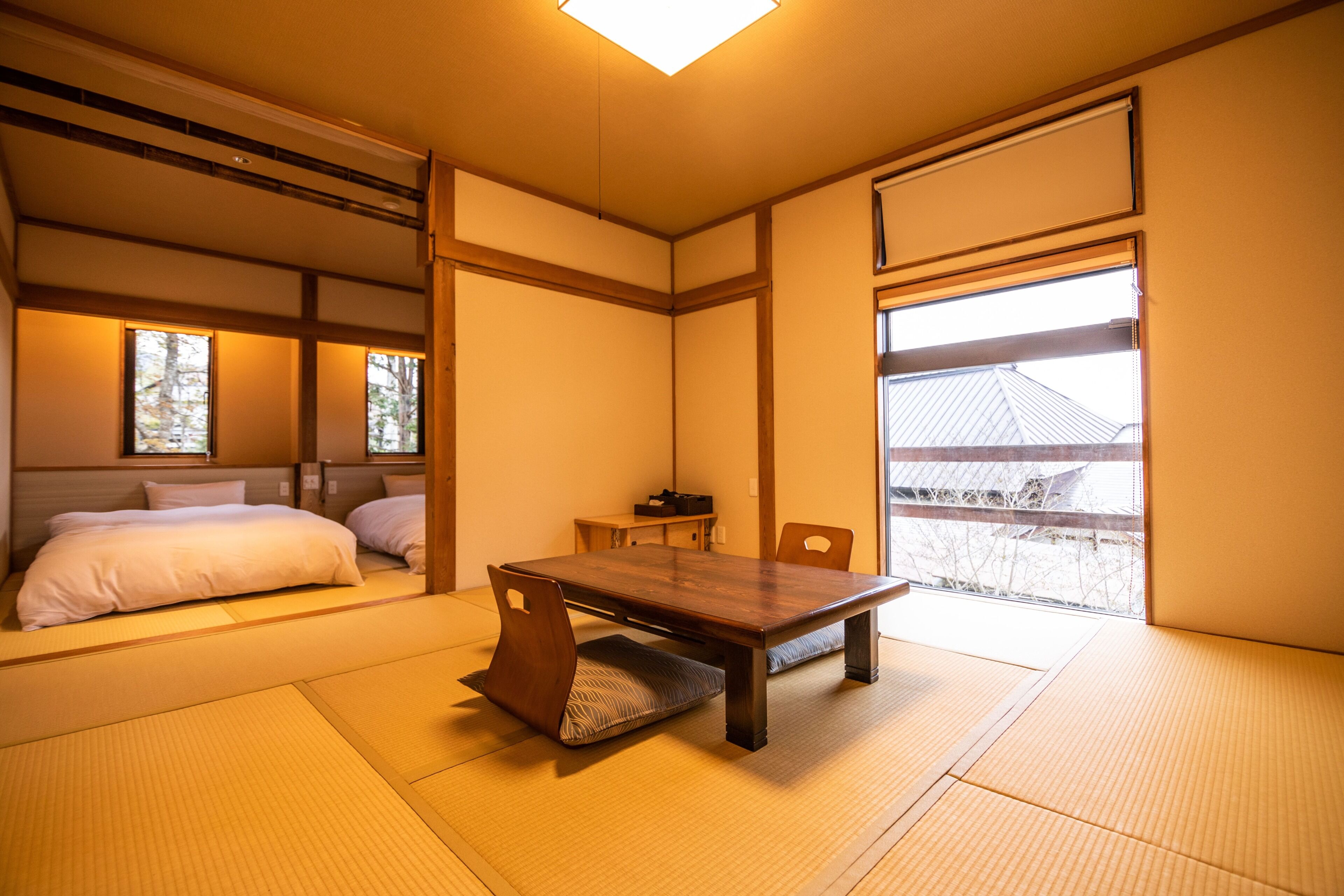 Um quarto japonês tradicional com tatames, uma mesa baixa e uma cama com almofadas.