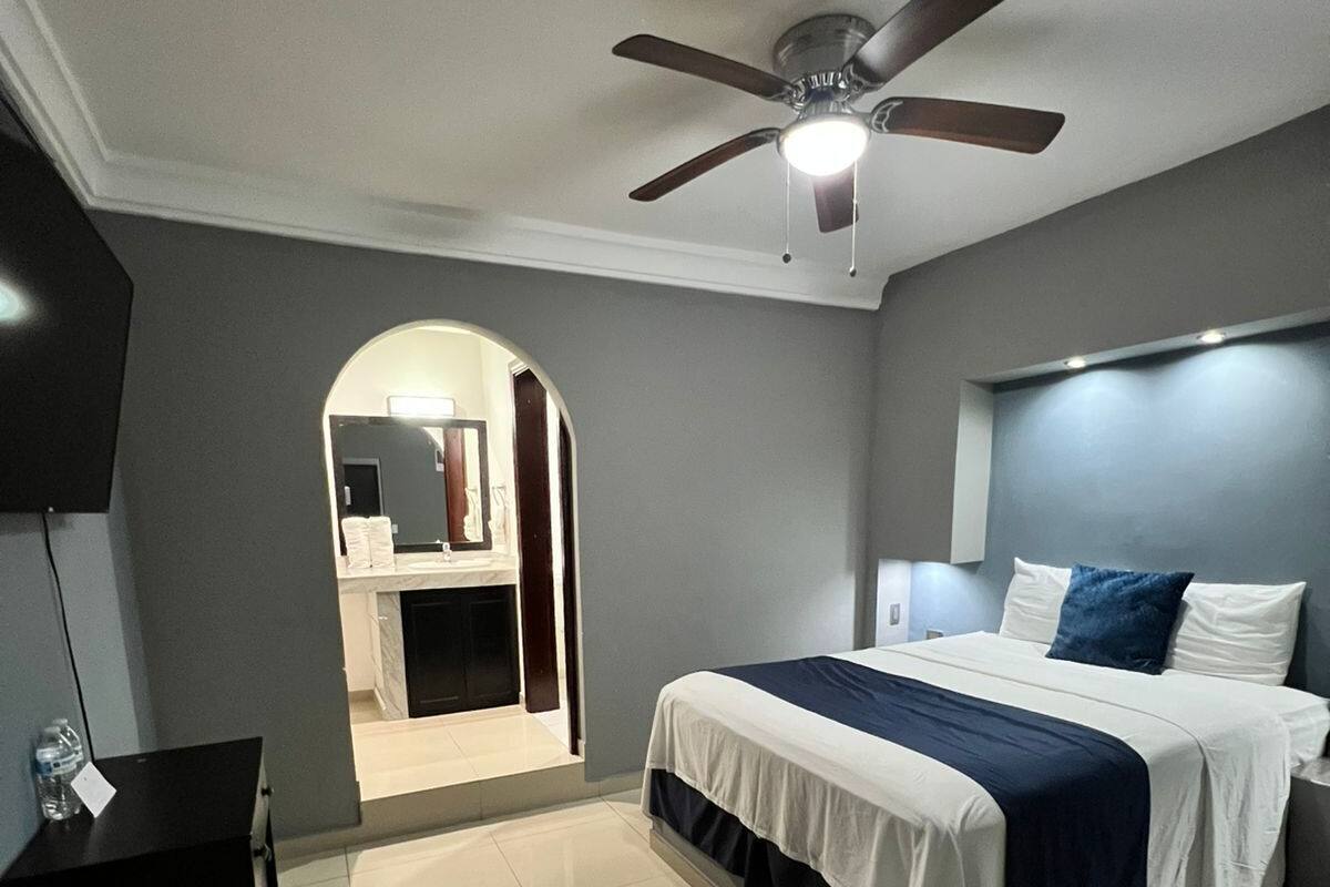 Quarto com cama, ventoinha no teto, televisão e escrivaninha.