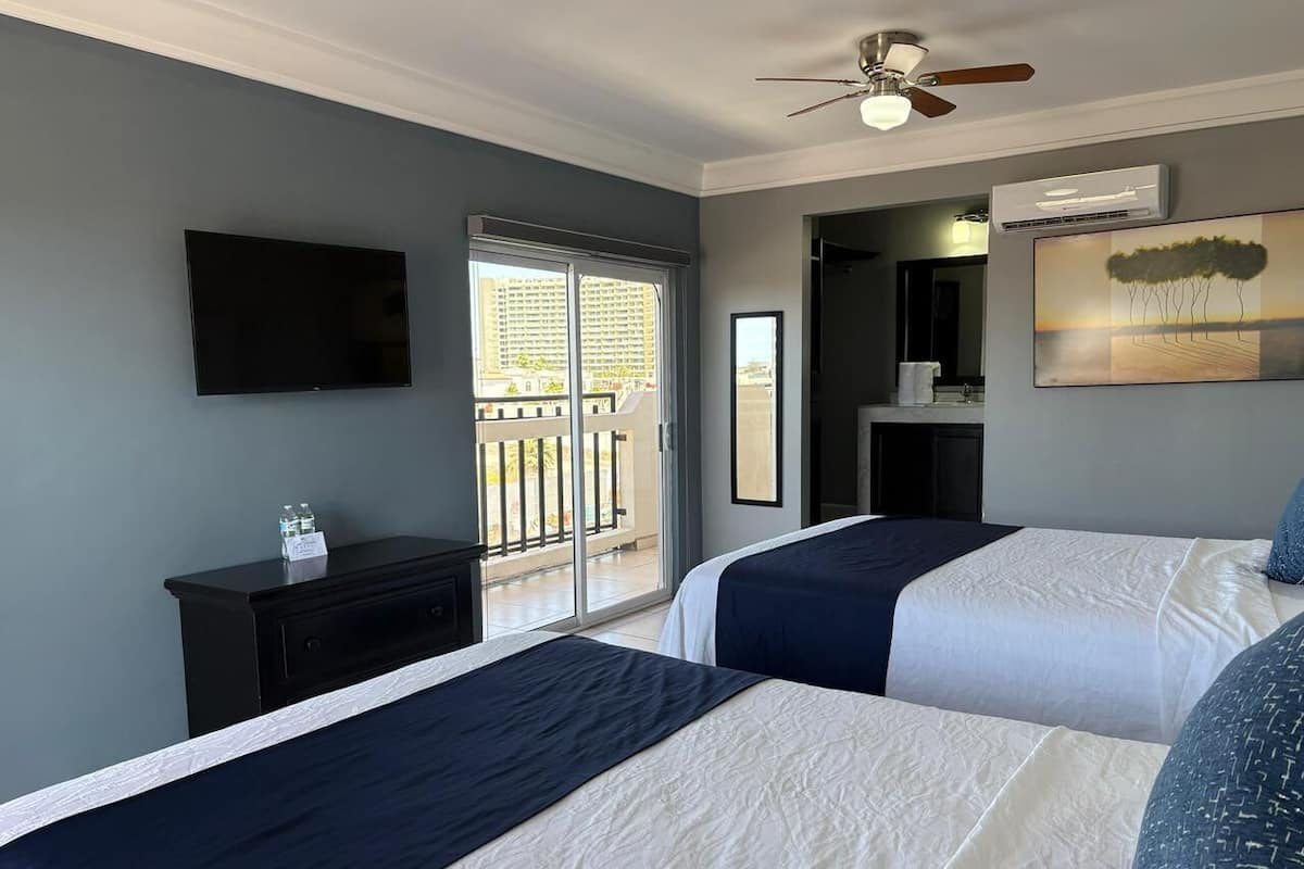 Quarto de hotel com duas camas, televisão, cômoda e varanda com vista.