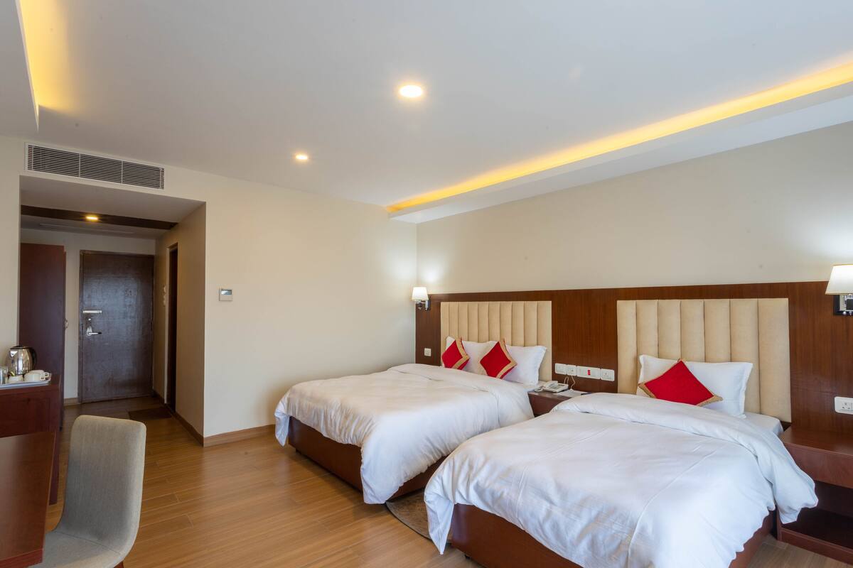 Quarto de hotel com duas camas, piso de madeira, uma escrivaninha e uma cadeira.