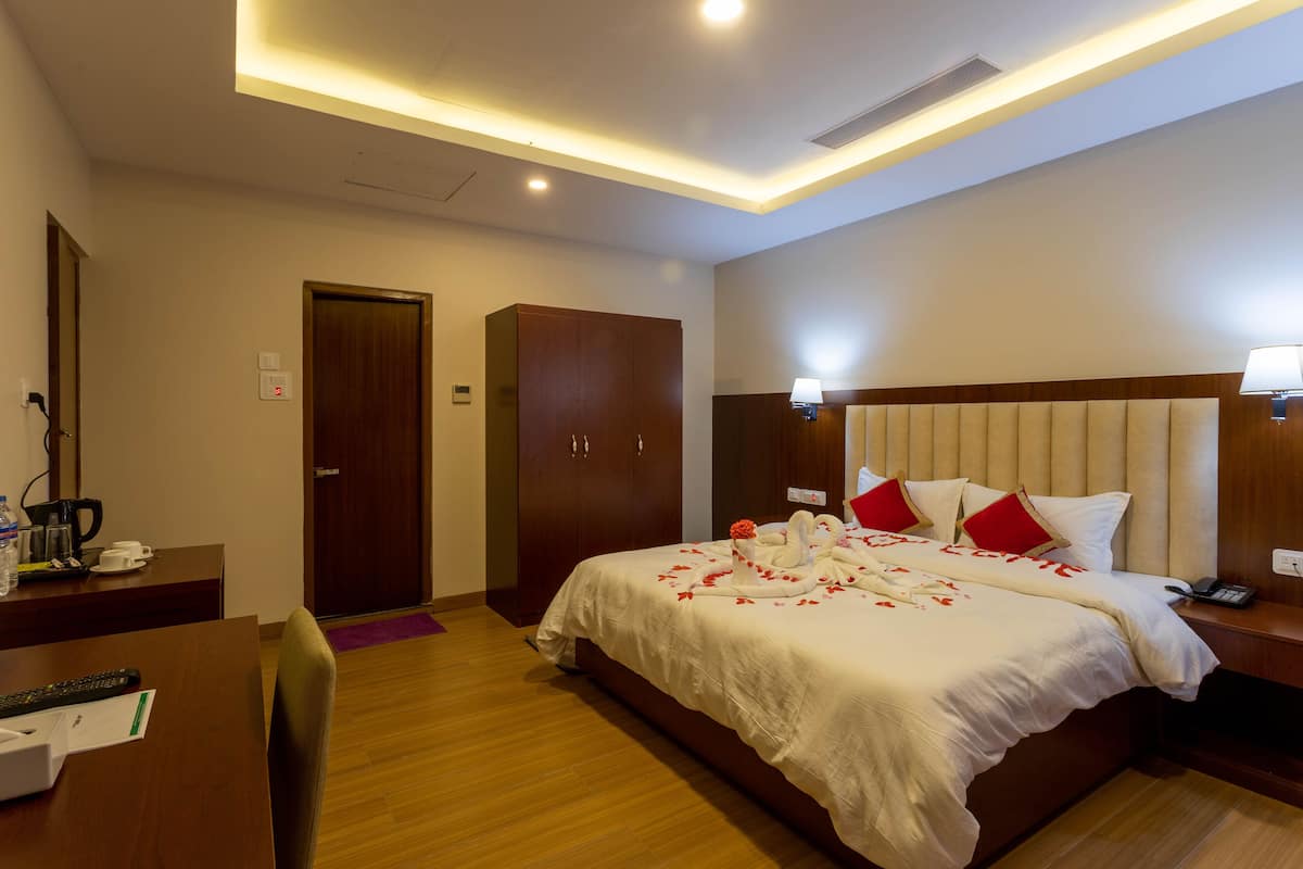 Quarto de hotel com cama, mesa de cabeceira, luminária e escrivaninha com cadeira.