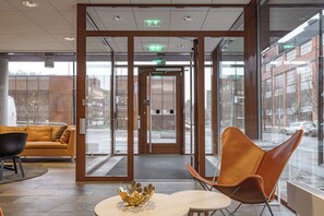 Um lobby moderno com entrada por porta de vidro, um sofá, uma poltrona e uma mesa com uma tigela decorativa.