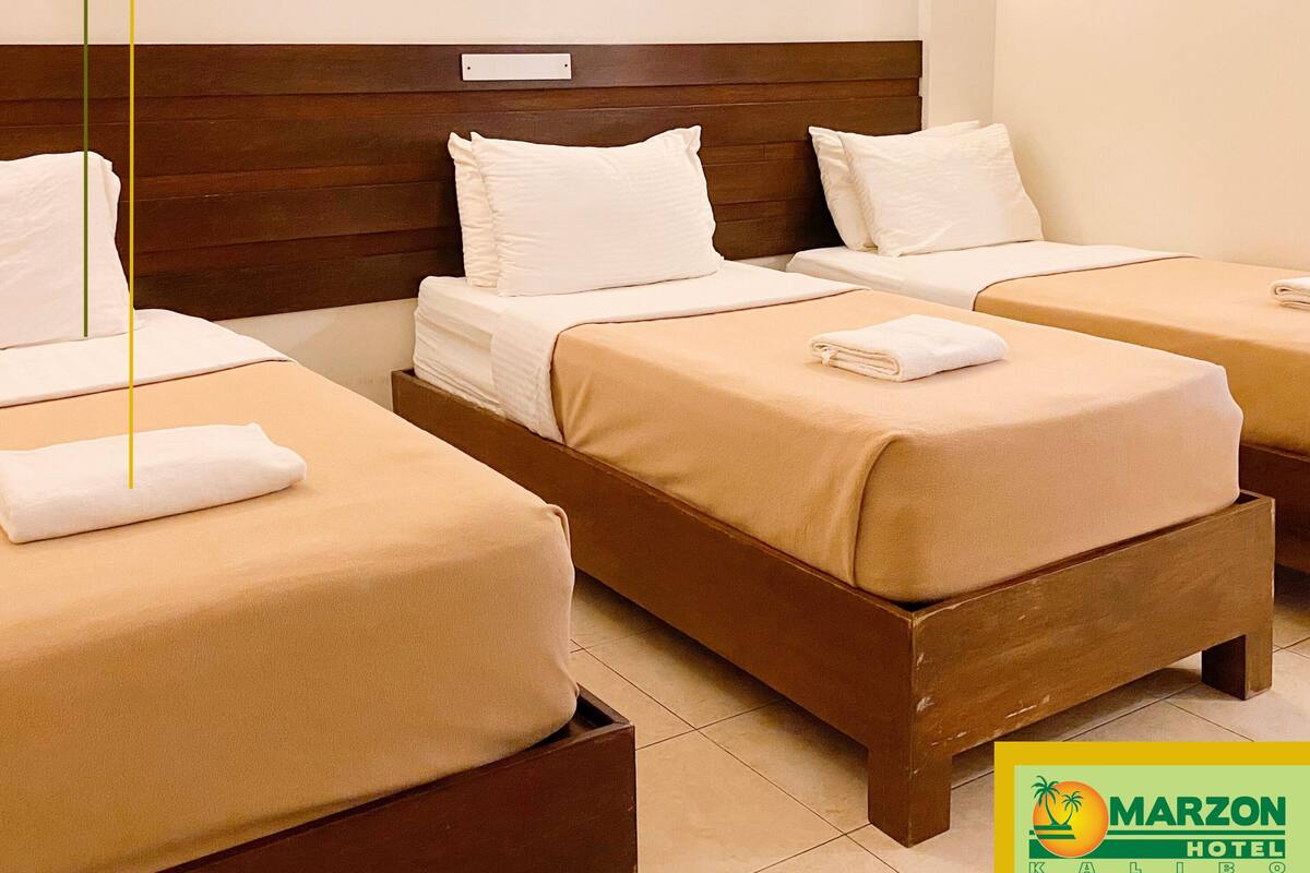 Quarto de hotel com duas camas de solteiro, cabeceira de madeira, quadro na parede e mesa de cabeceira com luminária.