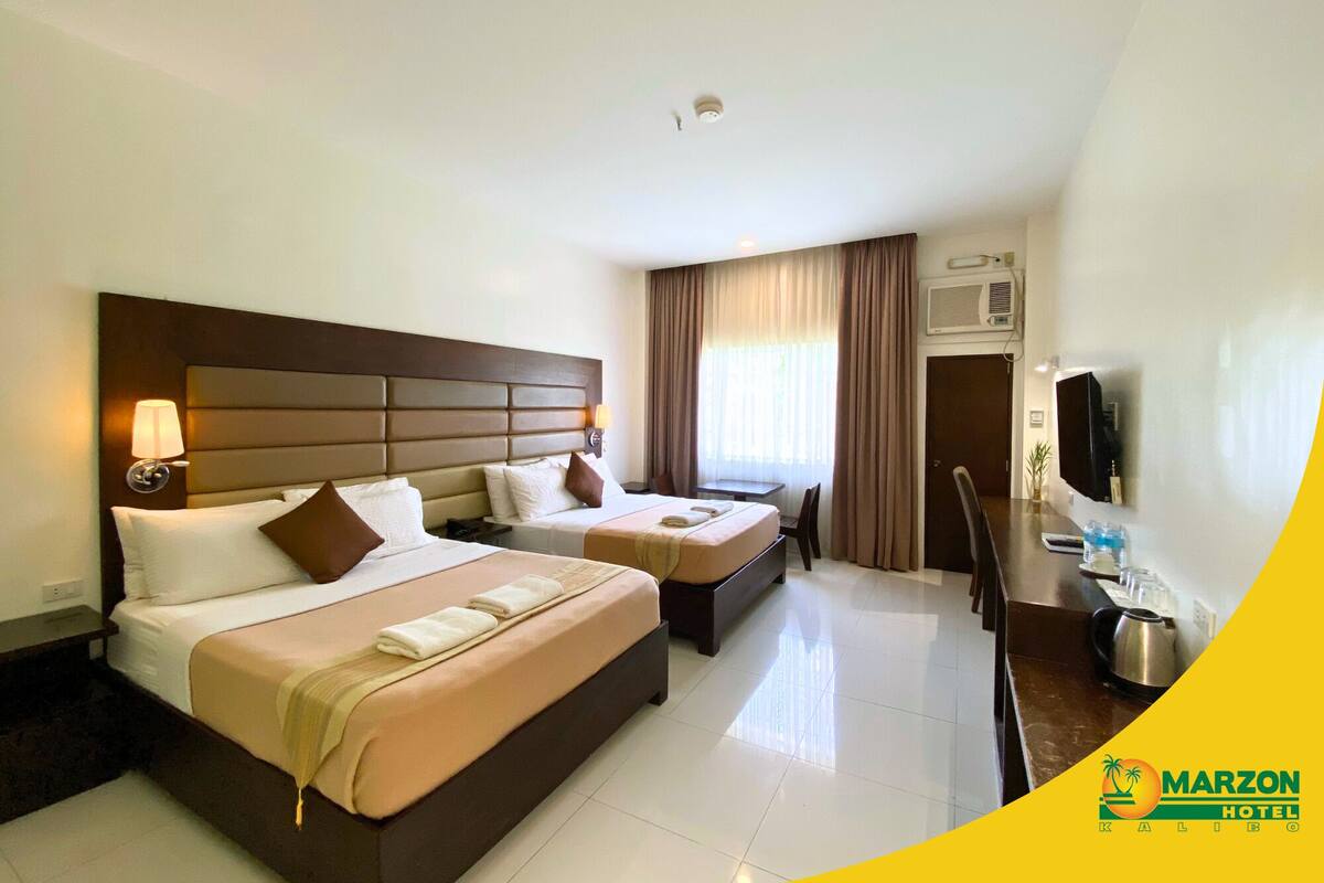 Quarto de hotel com duas camas, uma mesa, uma televisão e um minibar.