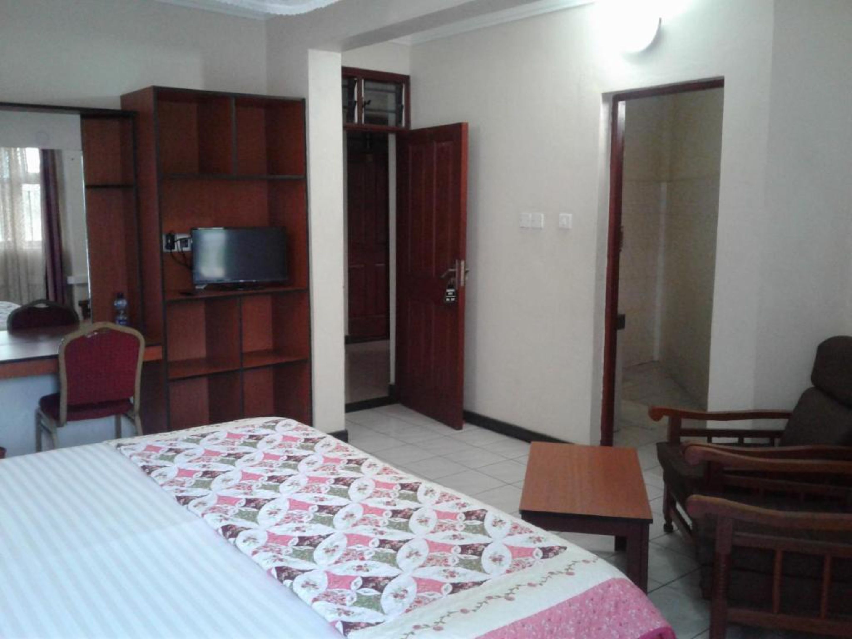 Quarto de hotel com cama, secretária com computador, televisão, armário e cadeira.
