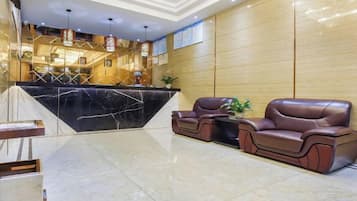 Um saguão de hotel com balcão de recepção, assentos de couro e uma parede decorativa.