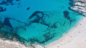 Vista aérea de uma praia com águas turquesa cristalinas e afloramentos rochosos.