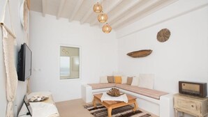 Uma sala de estar com um sofá branco, uma mesa de centro de madeira, uma televisão em um suporte e um objeto decorativo na parede.