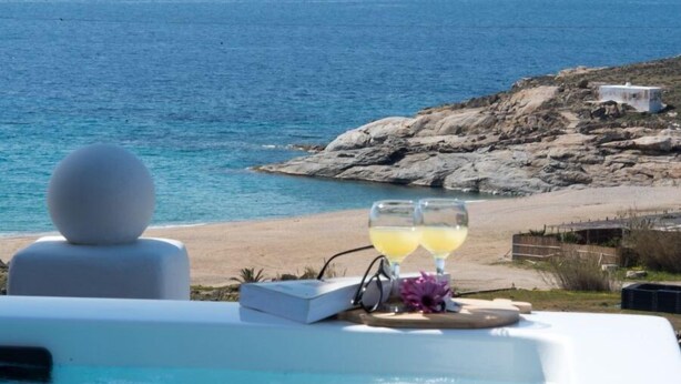 Vista da piscina com visão clara do mar, um afloramento rochoso e um pequeno edifício.