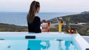 Uma pessoa num bar à beira da piscina, com vista para a paisagem costeira, o mar e as colinas.
