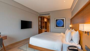 Quarto de hotel moderno com uma cama grande, uma escrivaninha, televisão de ecrã plano, cabeceira de madeira e uma obra de arte na parede.