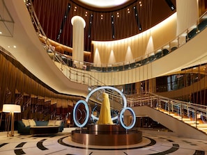 Interior com vários níveis, uma luminária circular central, guarda-corpos de vidro e uma escadaria.