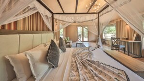 Quarto em estilo de tenda, com cama, travesseiros, uma mesinha e uma cadeira.