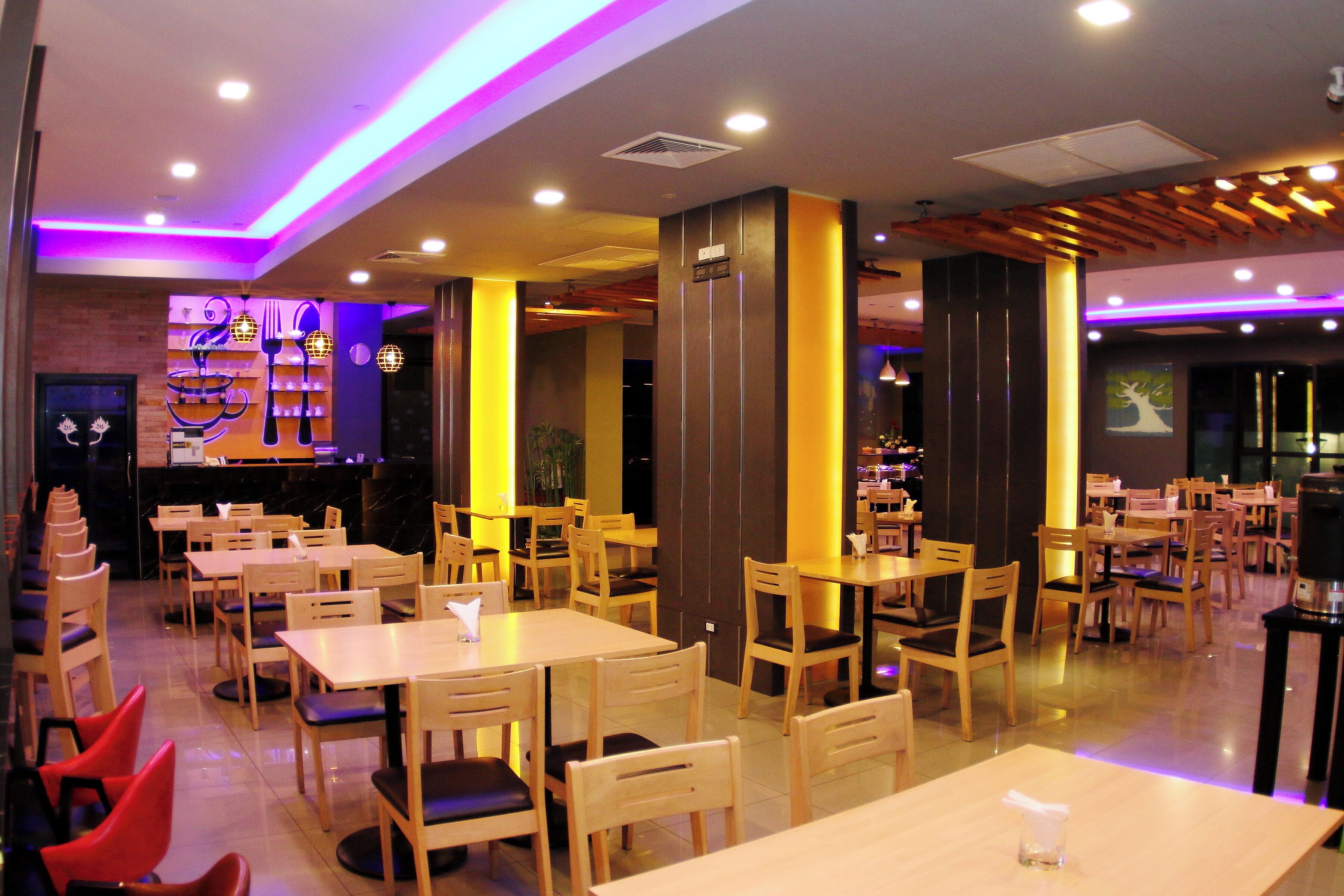 Um restaurante com mesas e cadeiras de madeira, área de bar e design de interiores moderno com detalhes em iluminação roxa.