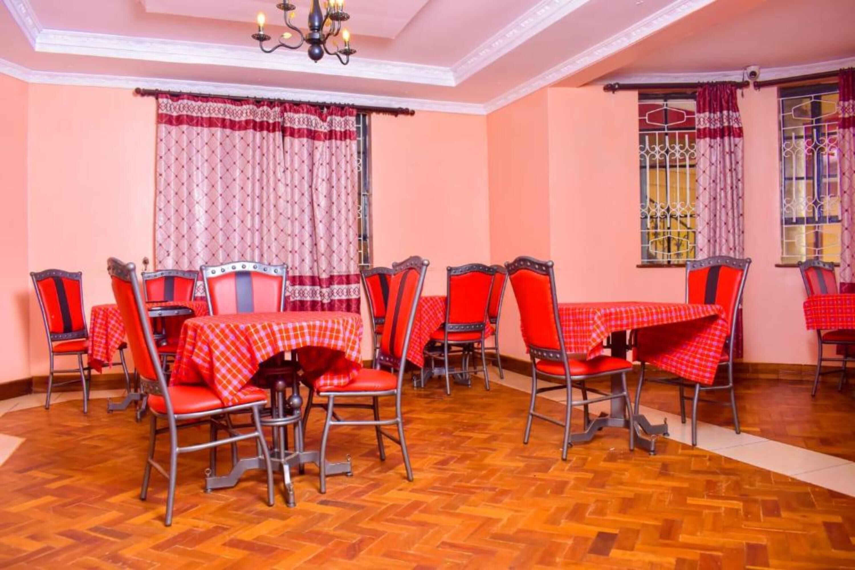 Uma sala de jantar com cadeiras e mesas vermelhas, piso de madeira e cortinas decorativas.