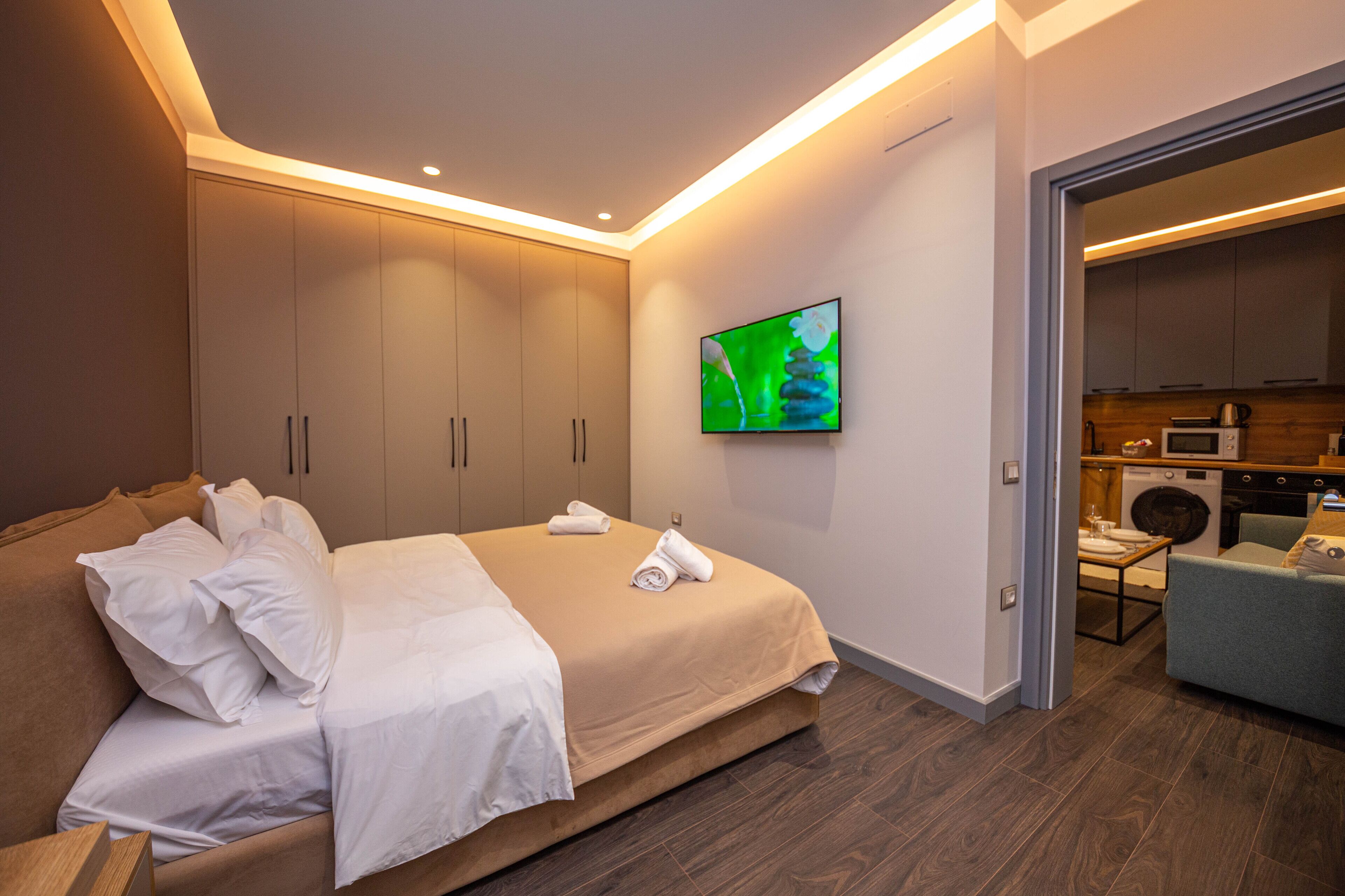 Quarto de hotel moderno com uma cama grande, televisão de tela plana, máquina de lavar e cozinha compacta.