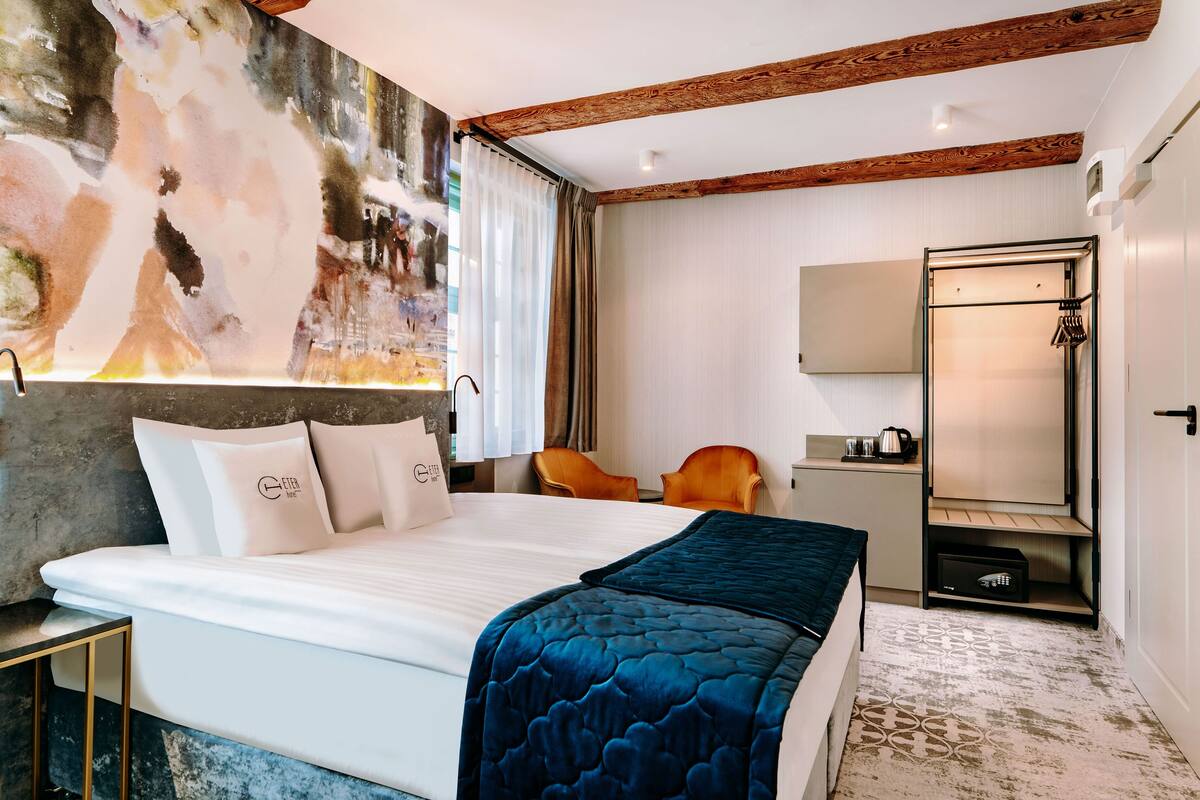 Quarto de hotel moderno com uma cama grande, área de chuveiro e espaço de estar com cadeiras.