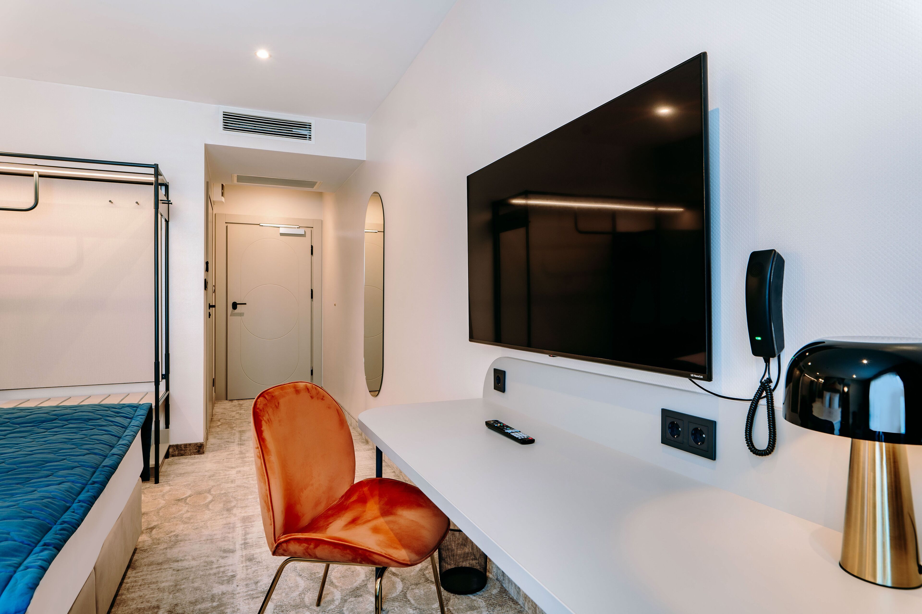 Quarto de hotel com cama, escrivaninha, cadeira, televisão e telefone.