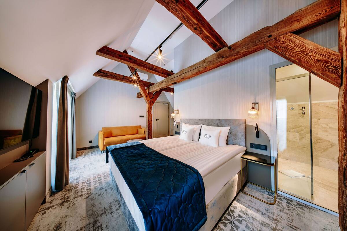 Quarto moderno com uma cama grande, vigas de madeira, um sofá e um closet espaçoso.