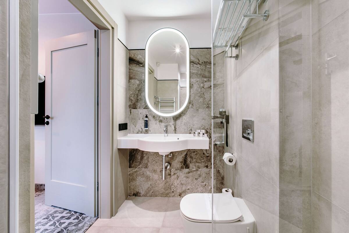 Uma casa de banho moderna com chuveiro de vidro, parede de mármore e lavatório branco.