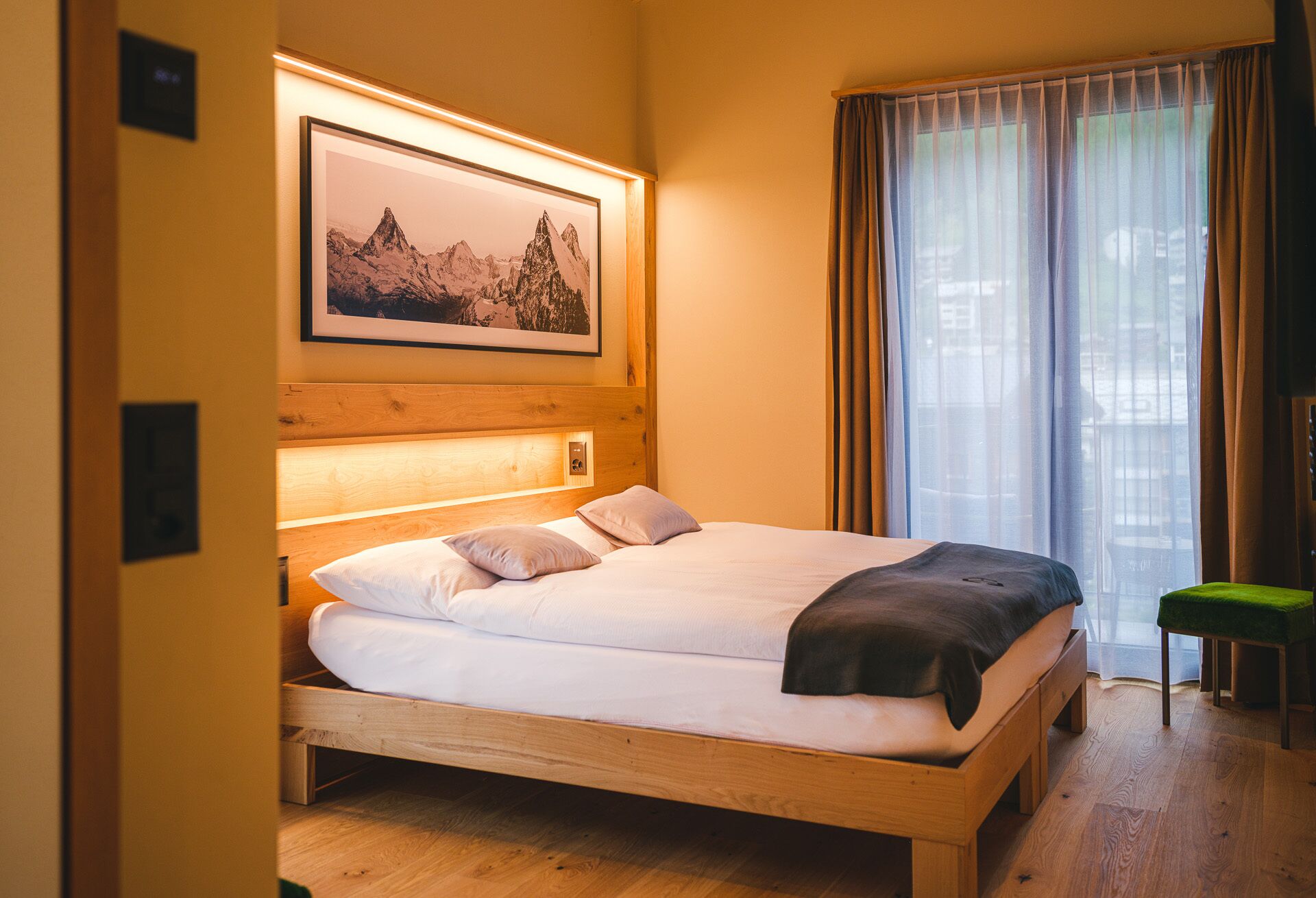Cama bem arrumada com cabeceira, um quadro emoldurado acima e uma janela com cortinas.