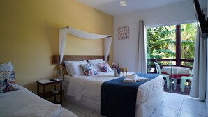 Quarto de hotel com duas camas, um ventilador de teto, varanda com mesa e cadeiras, e vista para o verde lá fora.