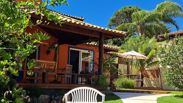 Uma casa com telhado em cerâmica, varanda com banco e um caminho que leva a uma palmeira.