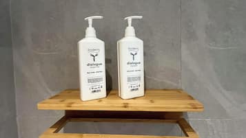 Dois frascos de gel de banho Boderm sobre uma prateleira de madeira, em frente a uma parede revestida de azulejos.