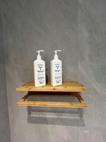 Dois frascos de gel de banho Boderm sobre uma prateleira de madeira, em frente a uma parede revestida de azulejos.