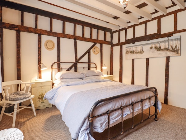 Quarto com estrutura de cama de metal, uma cadeira branca, mesa de cabeceira com abajur e um quadro na parede.