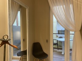 Quarto com um espelho grande, uma cadeira preta e vista para um pátio externo com mesa e cadeiras.