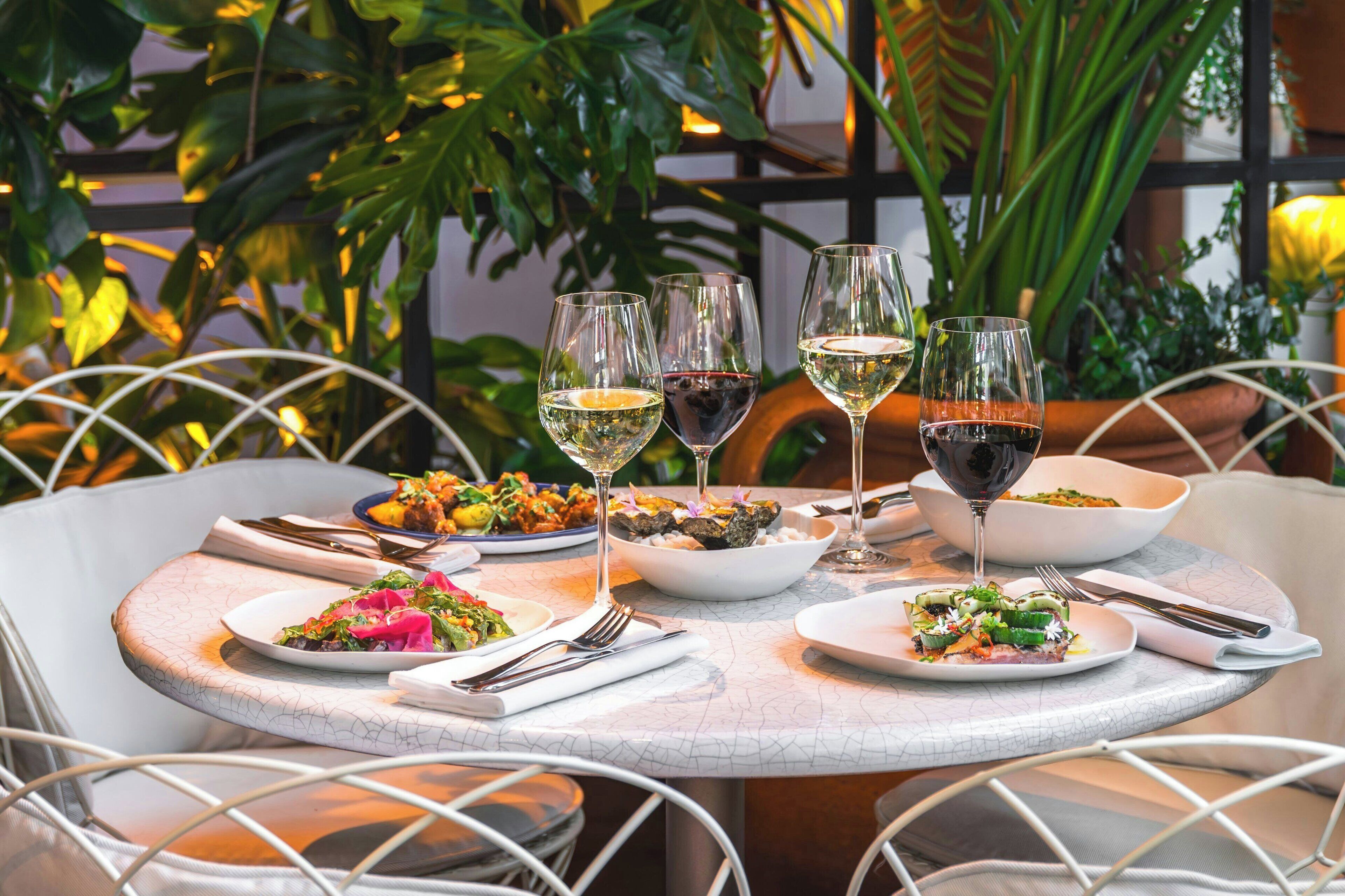 Uma mesa redonda com pratos de comida, copos de vinho e talheres.