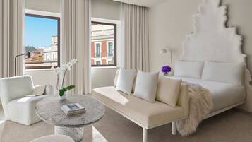 Quarto de hotel moderno com um sofá branco, uma mesa de centro redonda e vista da cidade através de amplas janelas.