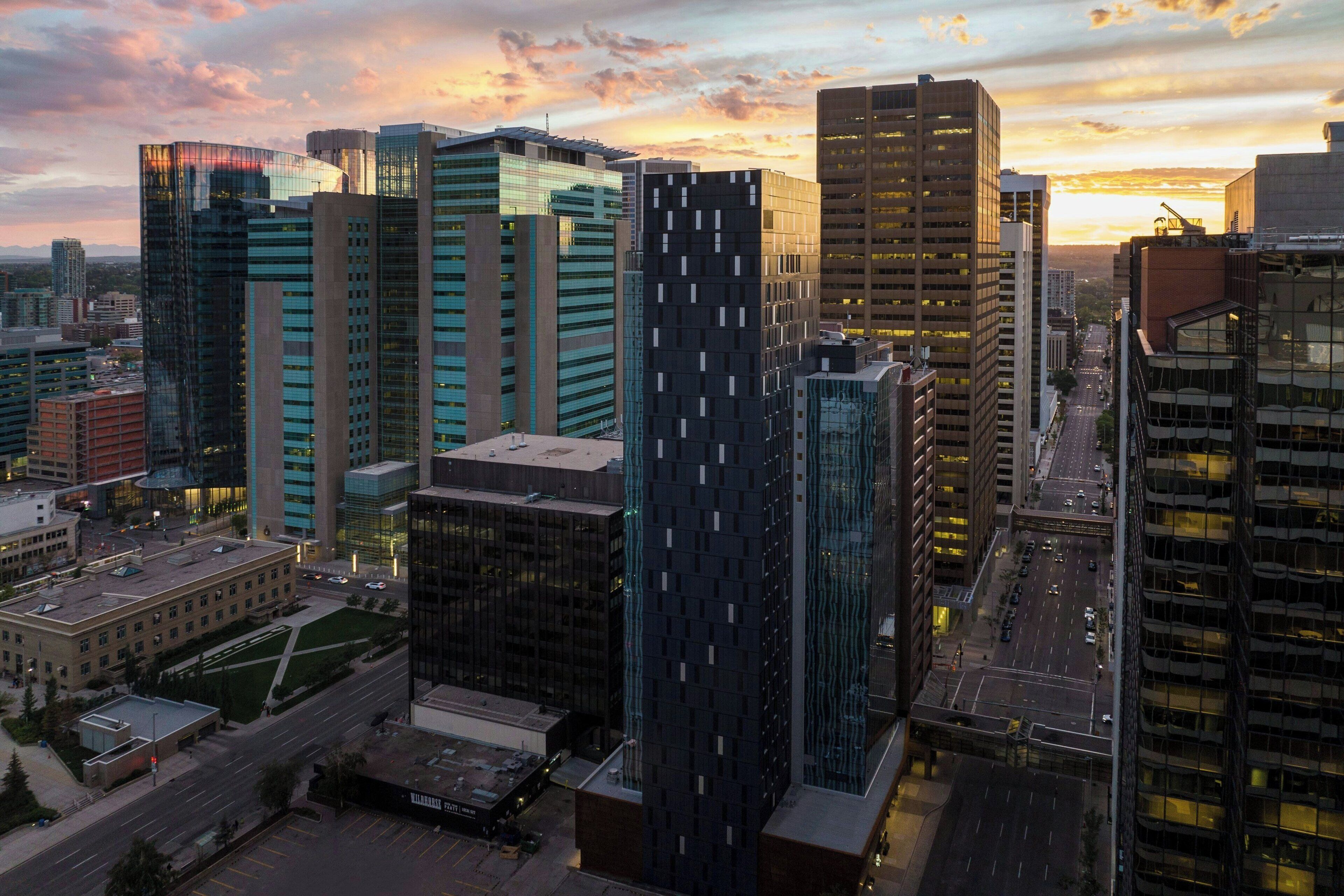 Paisagem urbana com edifícios modernos altos, um estacionamento e céu claro ao entardecer.